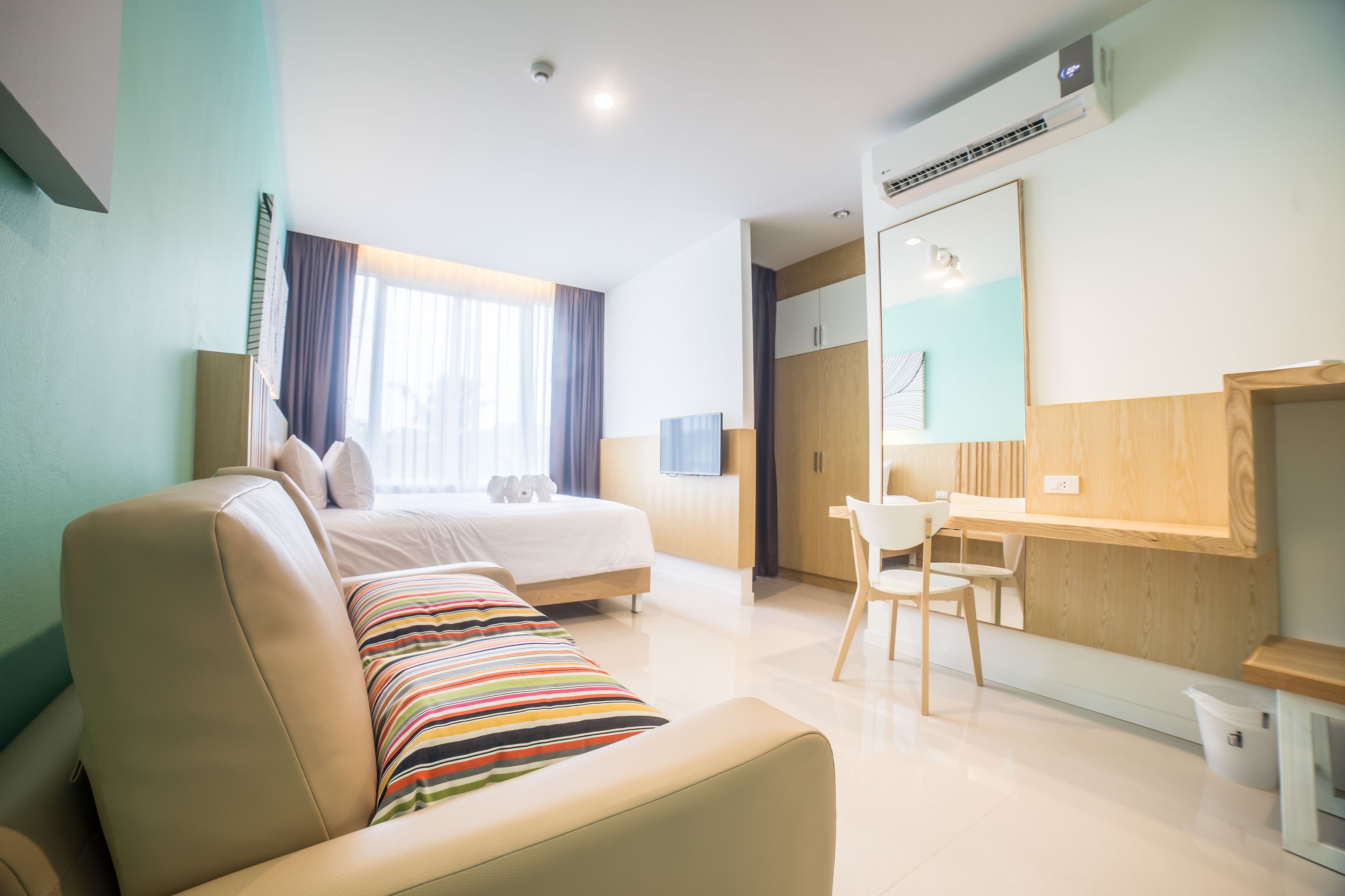 Quarto de hotel moderno com cama, sofá, escrivaninha e espelho.