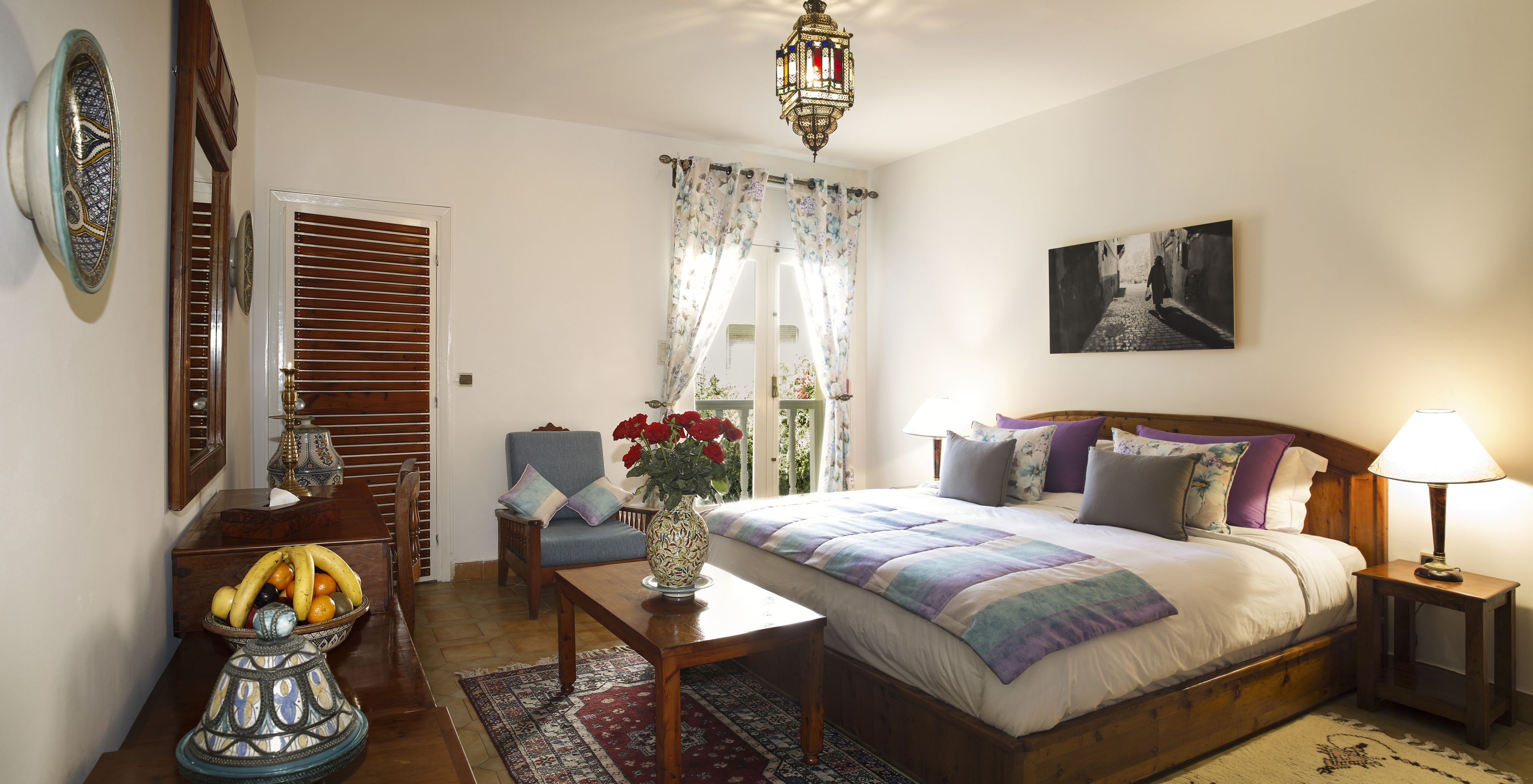 Quarto com cama, mesa de cabeceira, cadeira, mesa com frutas e um vaso de flores.