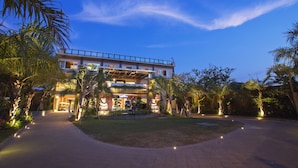 Um hotel com área externa coberta, palmeiras e um caminho pavimentado.