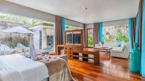 Quarto de hotel moderno com uma cama grande, um sofá, uma mesa de centro de madeira e uma televisão.