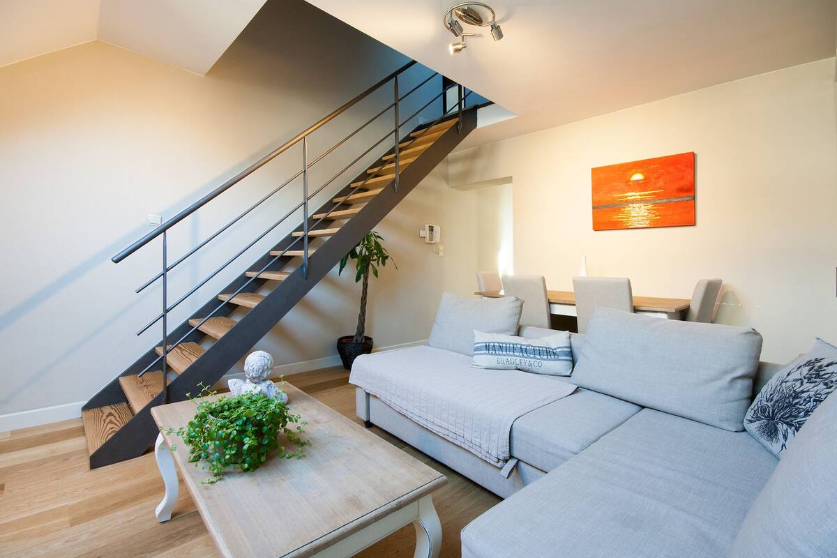 Uma sala de estar moderna com escada, sofá, mesa de centro e um quadro na parede.