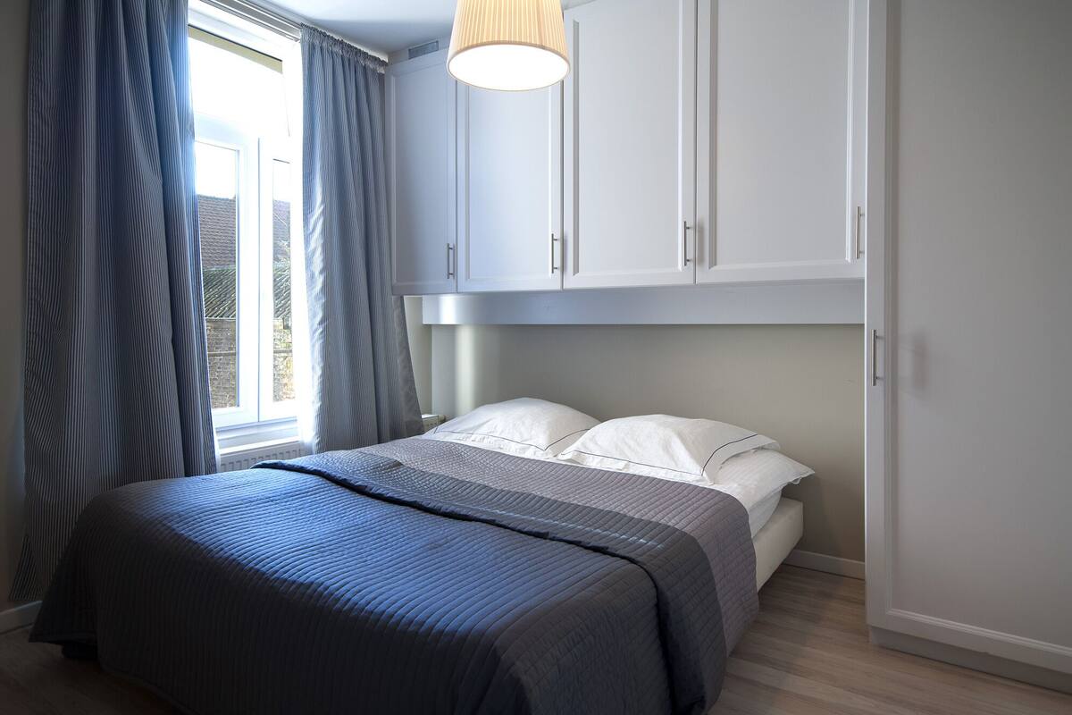Quarto com cama, cortinas brancas e janela.