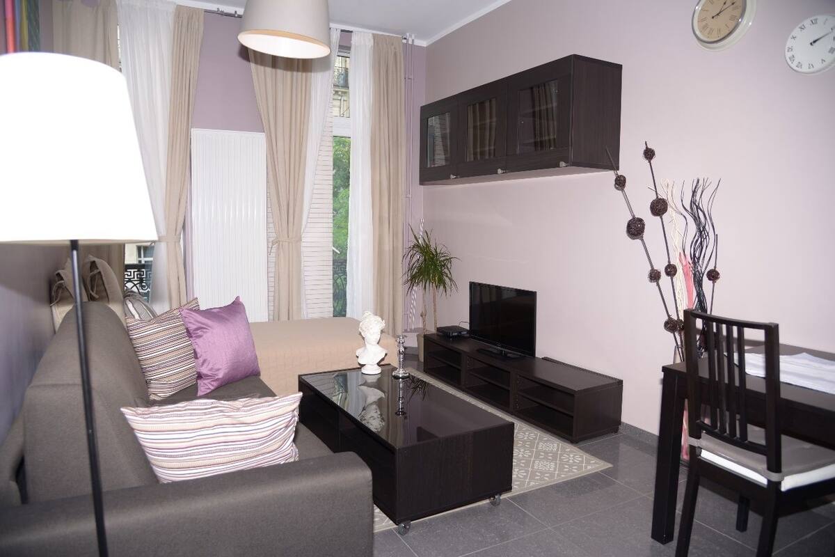 Uma sala de estar moderna com um sofá, mesa de centro, TV e uma área de refeições com cadeiras e uma mesa.
