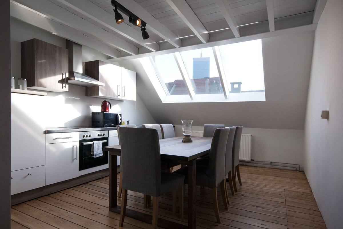 Uma cozinha moderna com armários brancos, fogão preto e área de jantar com mesa e cadeiras.