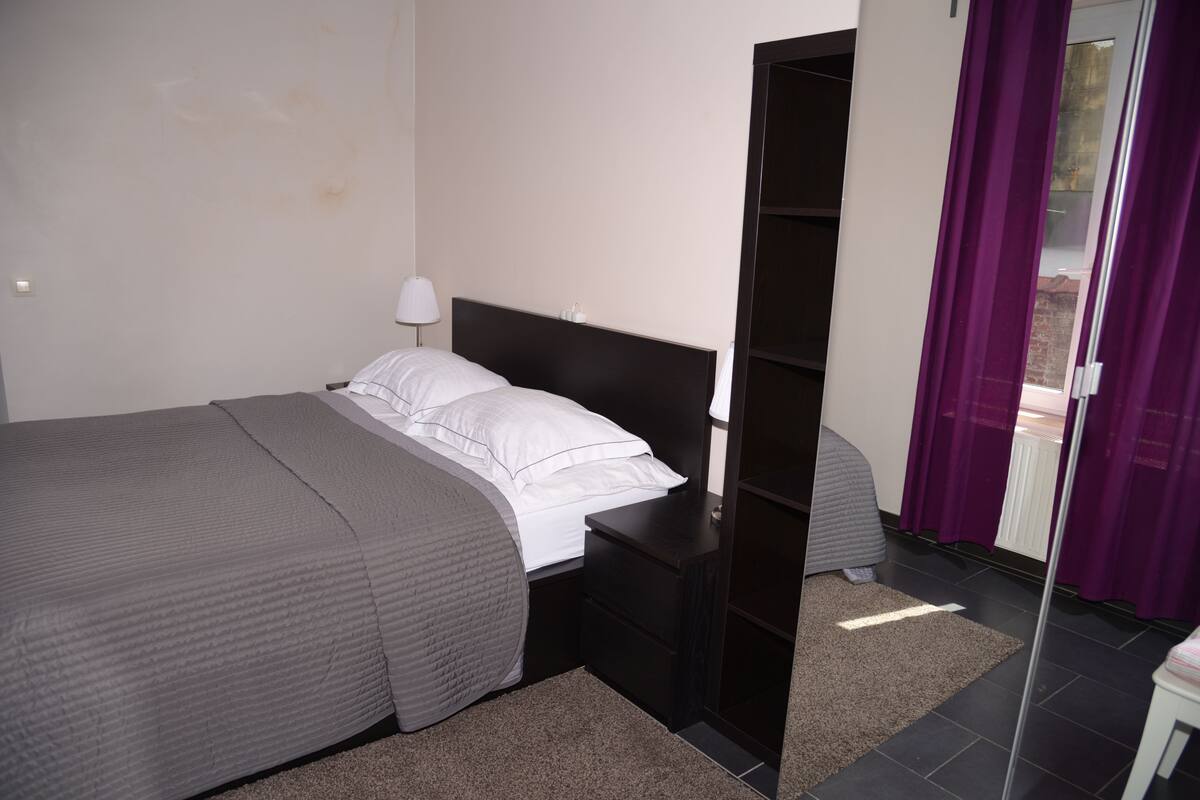 Quarto com cama, mesa de cabeceira, espelho e porta que dá para uma varanda.