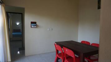 Quarto com mesa de madeira e cadeiras vermelhas, porta que dá para outro ambiente e interruptor de luz fixado na parede.