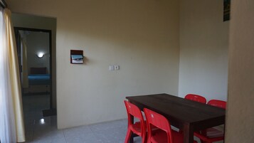 Quarto com mesa de madeira e cadeiras vermelhas, porta que dá para outro ambiente e interruptor de luz fixado na parede.
