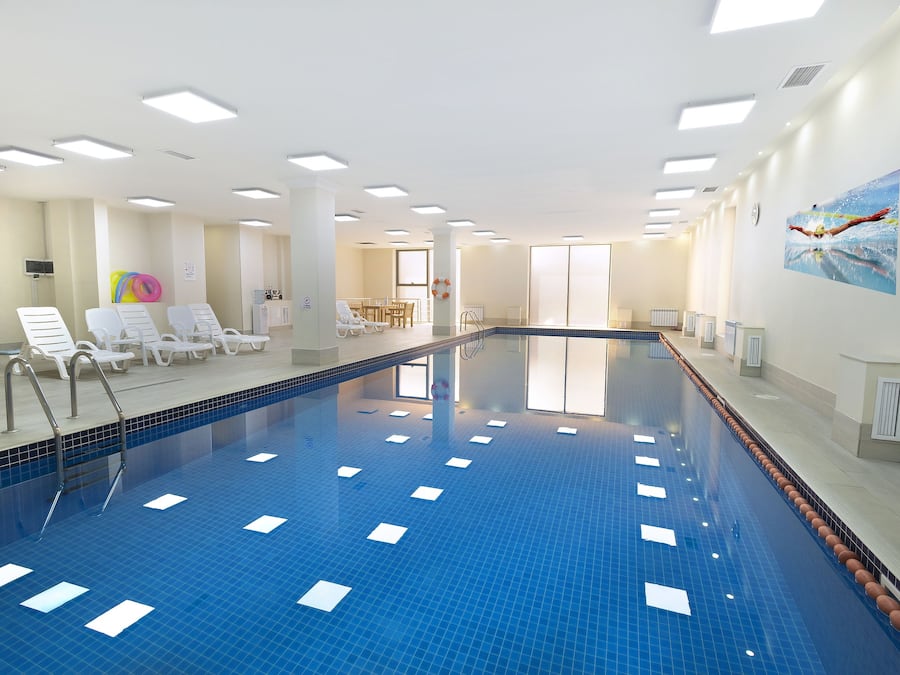 Piscina interior com pistas demarcadas, espreguiçadeiras e cadeira do salva-vidas.
