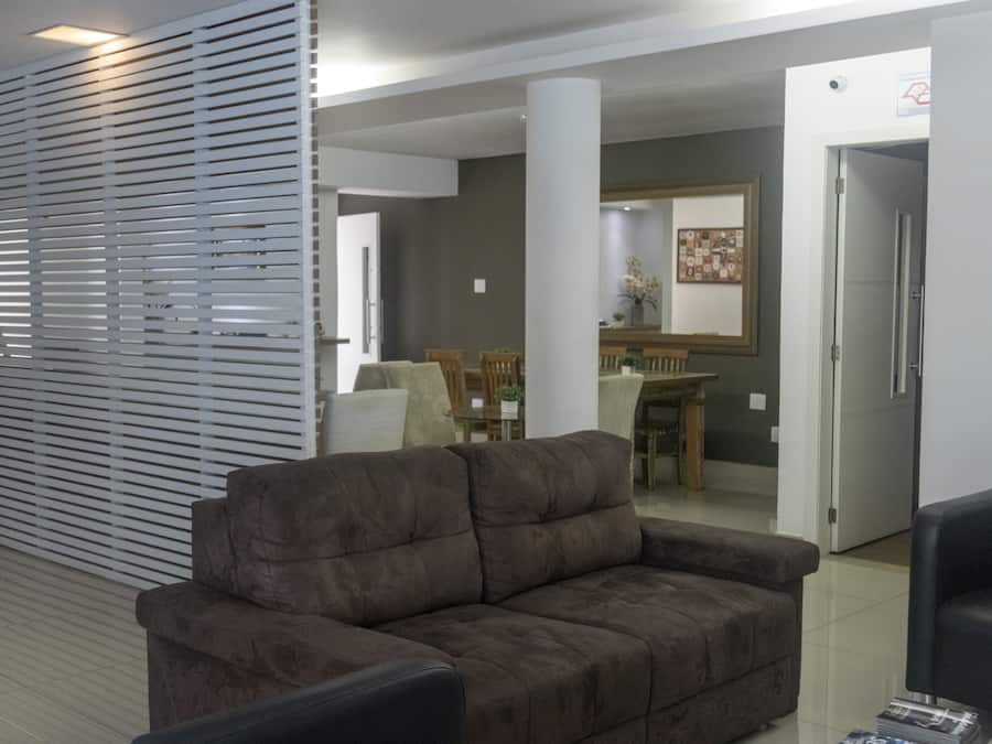Sala de estar com sofá marrom, área de jantar com mobiliário de madeira e cozinha visível por uma porta aberta.
