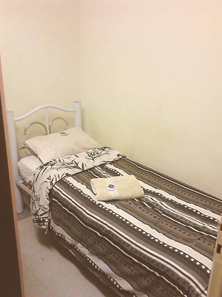Uma cama de solteiro com estrutura metálica, colcha estampada e um travesseiro.