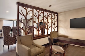 Quarto com divisória grande com padrão de árvore em madeira, televisão de tela plana na parede e mesa de jantar com cadeiras.