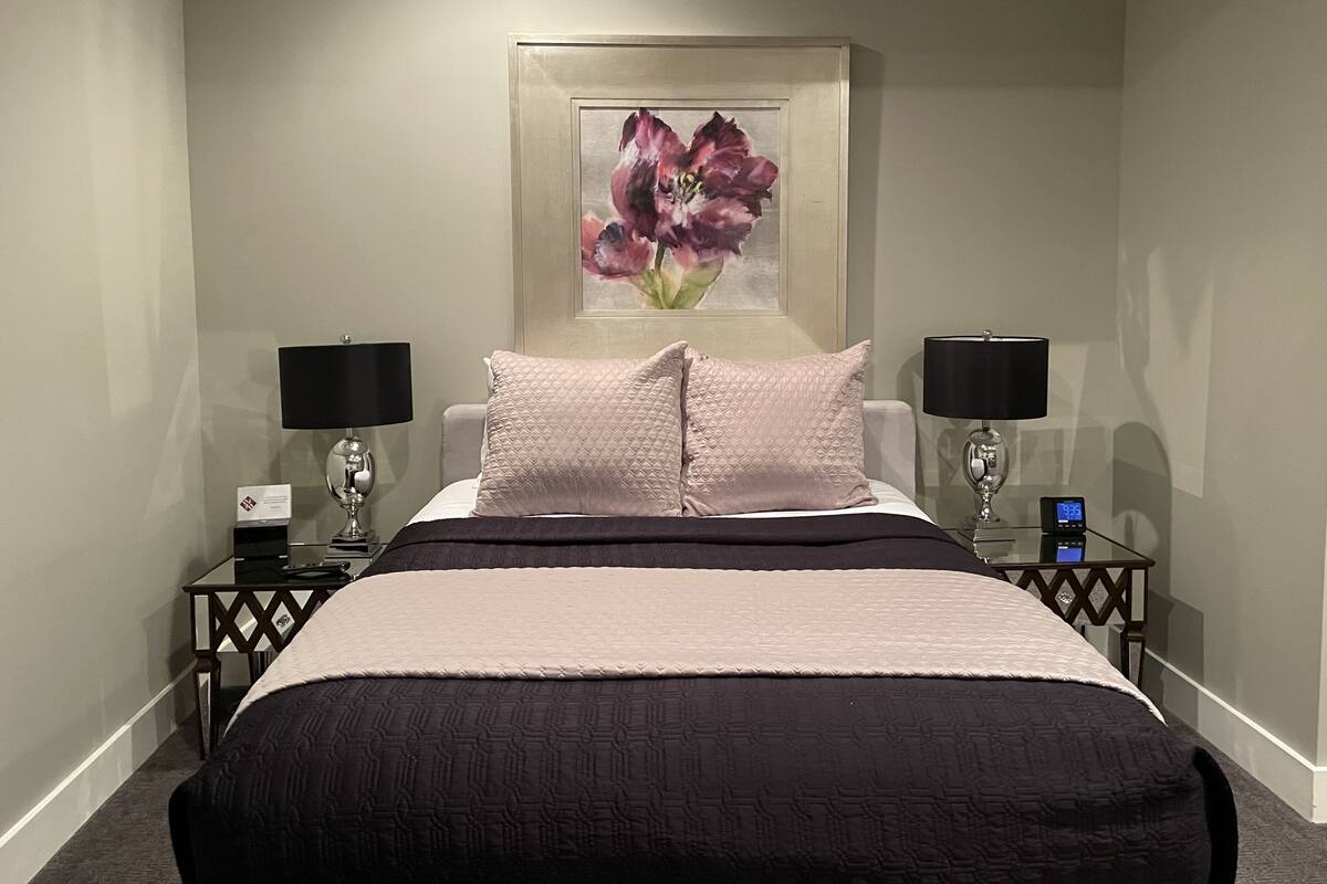 Quarto bem arrumado com uma cama, duas mesas de cabeceira, um criado-mudo, um relógio digital e uma pintura floral emoldurada na parede.