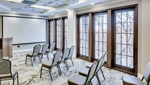 Uma sala de conferências com tela de projetor, amplas janelas e piso coberto de carpete.
