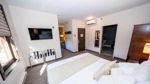 Quarto de hotel com uma cama grande, televisão de tela plana na parede, janela com persianas e porta que dá para um banheiro.