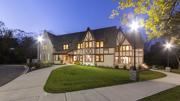 Uma grande casa em estilo Tudor, com dois andares, gramado bem cuidado e uma entrada com acesso por um caminho de acesso.