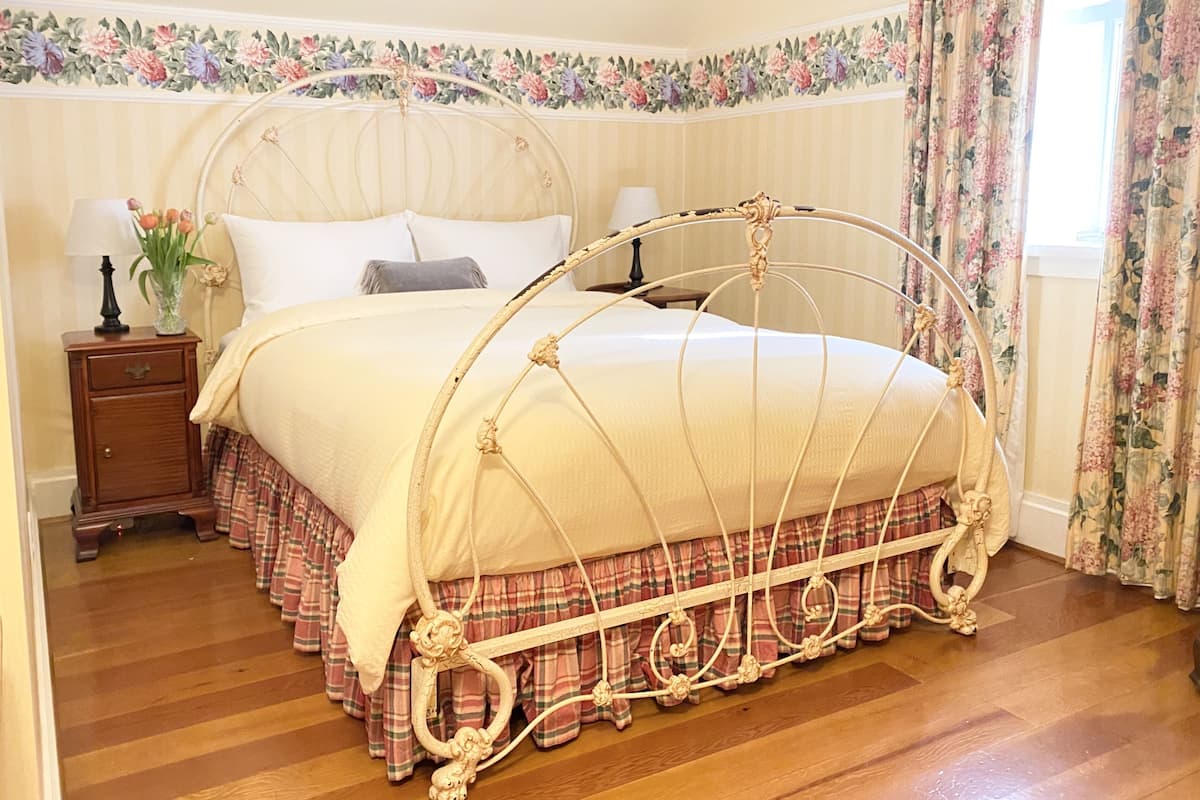 Quarto com uma cama de dossel, mesa de cabeceira com luminária e vaso, e papel de parede floral.