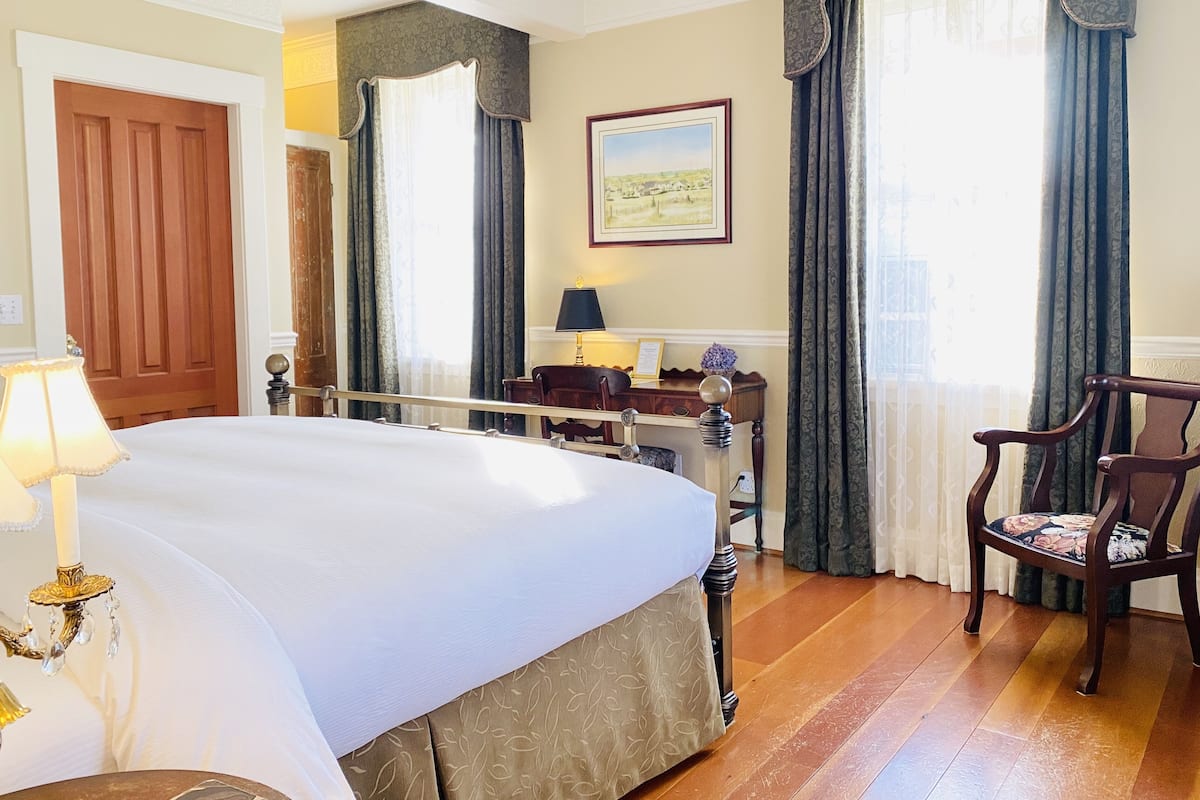 Quarto de hotel com uma cama grande, uma escrivaninha com luminária, uma cadeira e um quadro na parede.