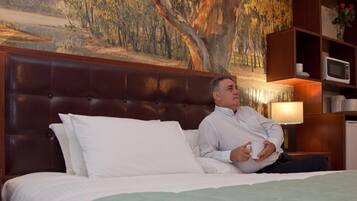 Quarto de hotel com cama grande, cabeceira, mesa de cabeceira, luminária, micro-ondas e uma pintura na parede.