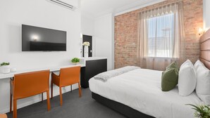 Quarto de hotel moderno com uma cama grande, uma mesa de escritório, duas cadeiras, uma TV de tela plana e uma parede de tijolos.