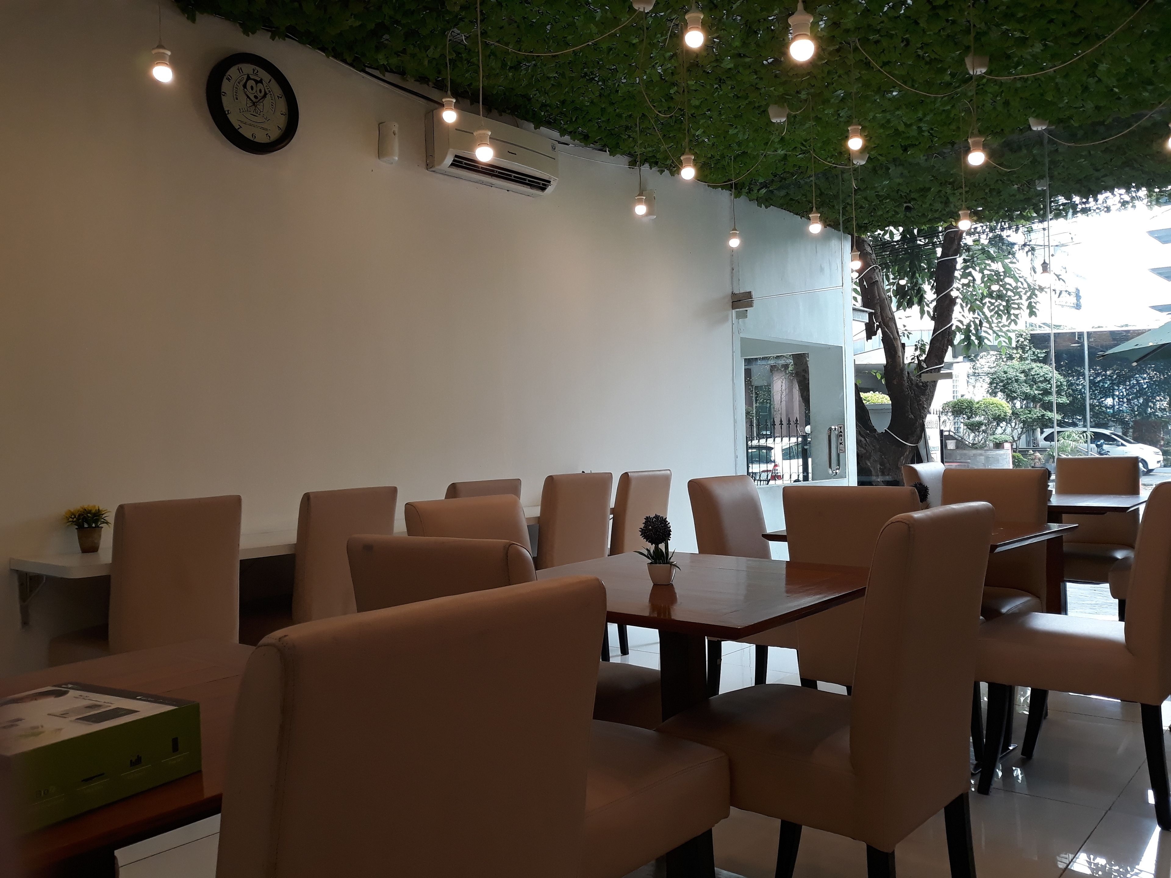 Interior de restaurante com mesas, cadeiras, um relógio na parede e luminárias pendentes.