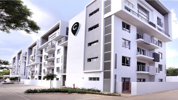 Um edifício residencial moderno de vários andares com varandas, um logotipo 'C' em destaque e uma entrada com portão.