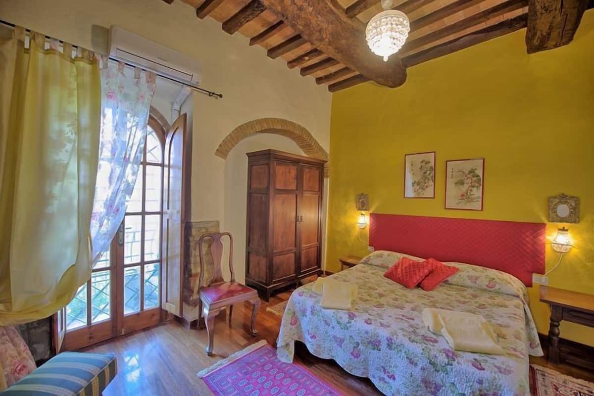 Quarto com cama, guarda-roupa de madeira, uma cadeira e janela com cortinas.