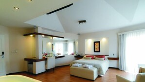 Quarto de hotel com uma cama grande, um espaço de estar com uma poltrona, uma mesa pequena, uma banheira e um espelho amplo.