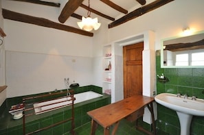 Casa de banho com um banco de madeira, uma banheira, uma pia e um revestimento de azulejos verdes.
