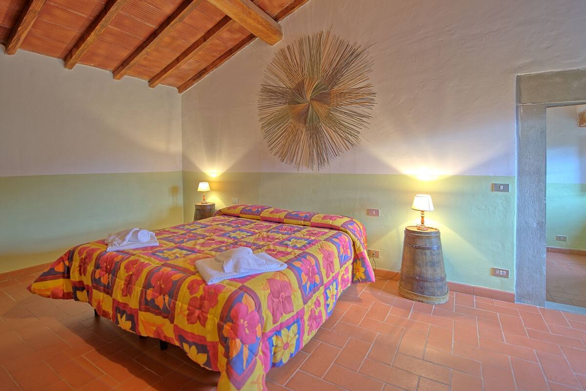 Quarto com uma cama grande, duas luminárias de cabeceira, um objeto decorativo na parede e piso de azulejos.