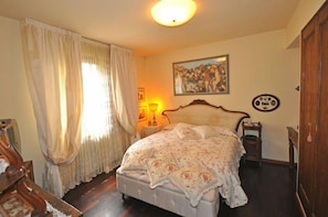 Quarto com cama, cortinas, um quadro, um abajur e um armário de madeira.