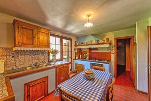 Uma cozinha com armários de madeira, toalha de mesa xadrez e um lustre.