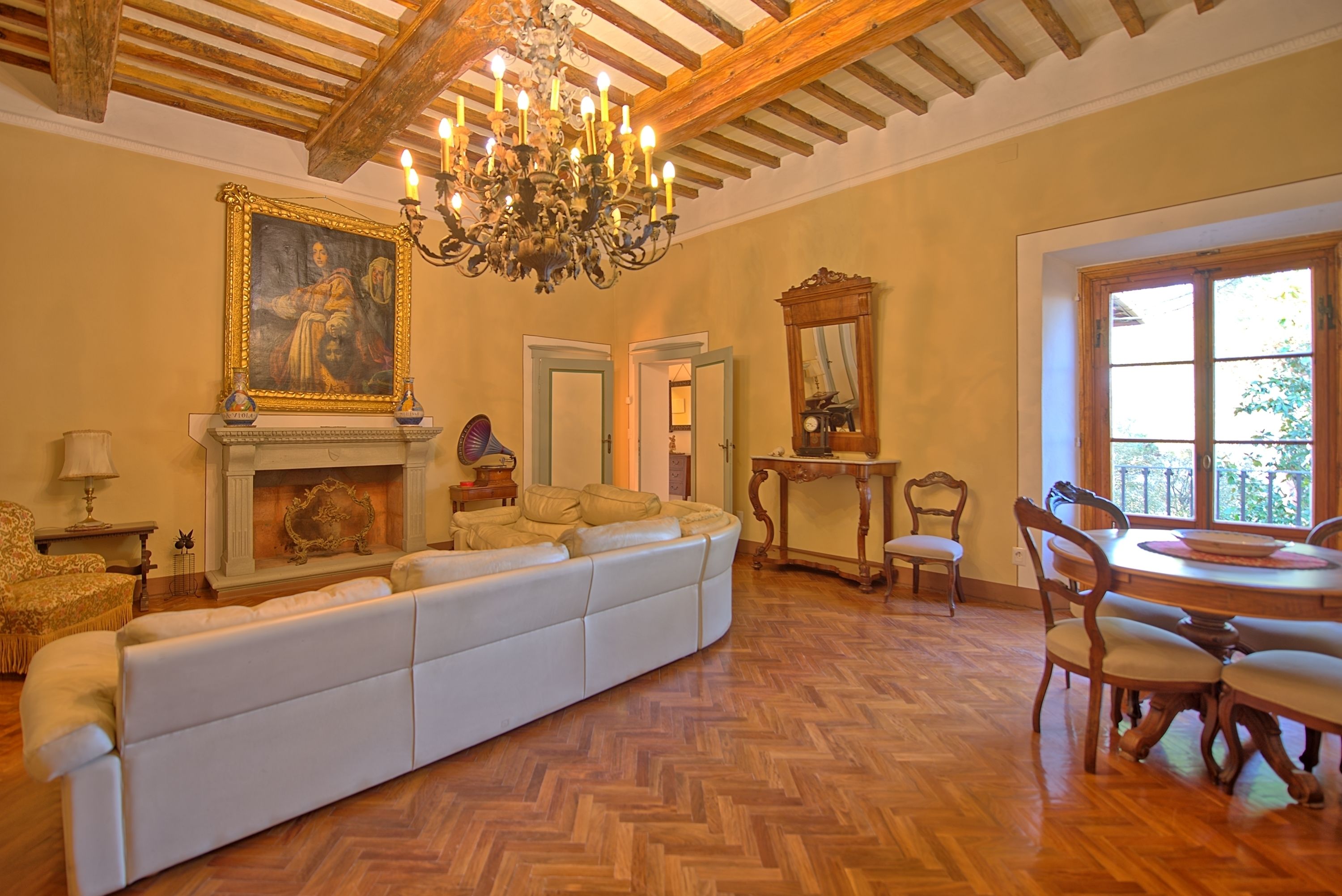 Uma sala de estar espaçosa com um sofá branco, piso de madeira, um candelabro, lareira e um espaço de jantar com cadeiras e mesa de madeira.