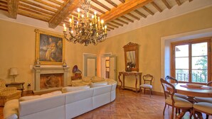 Uma sala de estar espaçosa com um sofá branco, piso de madeira, um candelabro, lareira e um espaço de jantar com cadeiras e mesa de madeira.