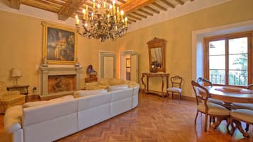 Uma sala de estar espaçosa com um sofá branco, piso de madeira, um candelabro, lareira e um espaço de jantar com cadeiras e mesa de madeira.