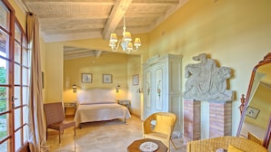 Quarto com cama, cadeira, mesa, guarda-roupa e uma estátua.