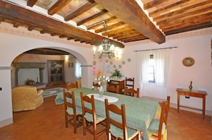 Uma área de refeições com uma mesa e cadeiras de madeira, um candelabro e vista para outro cômodo.