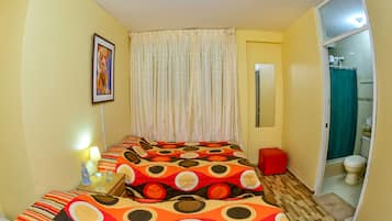 Quarto de hotel com duas camas, banheiro e um banquinho vermelho.
