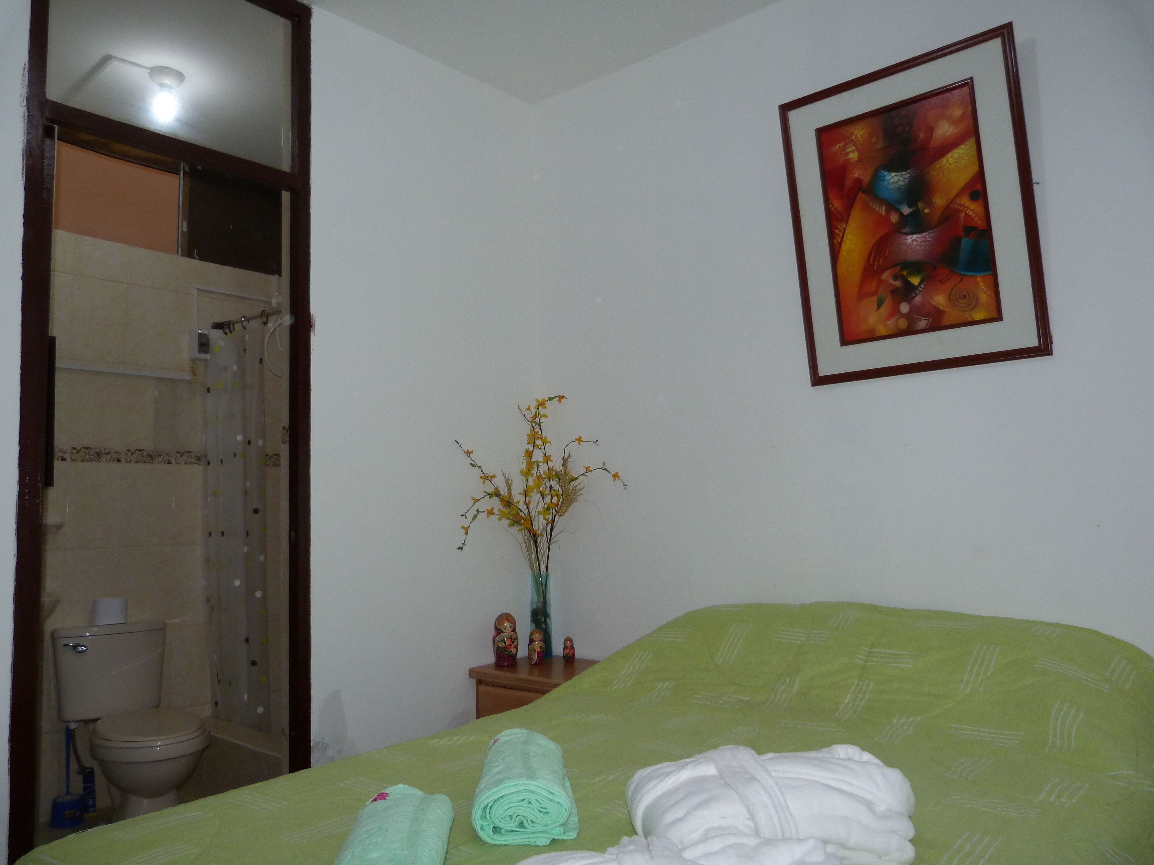 Quarto de hotel com cama, banheiro, um quadro na parede e um vaso com flores.