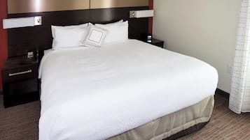 Quarto de hotel com uma cama grande, cabeceira de madeira, mesa de cabeceira e cortina.