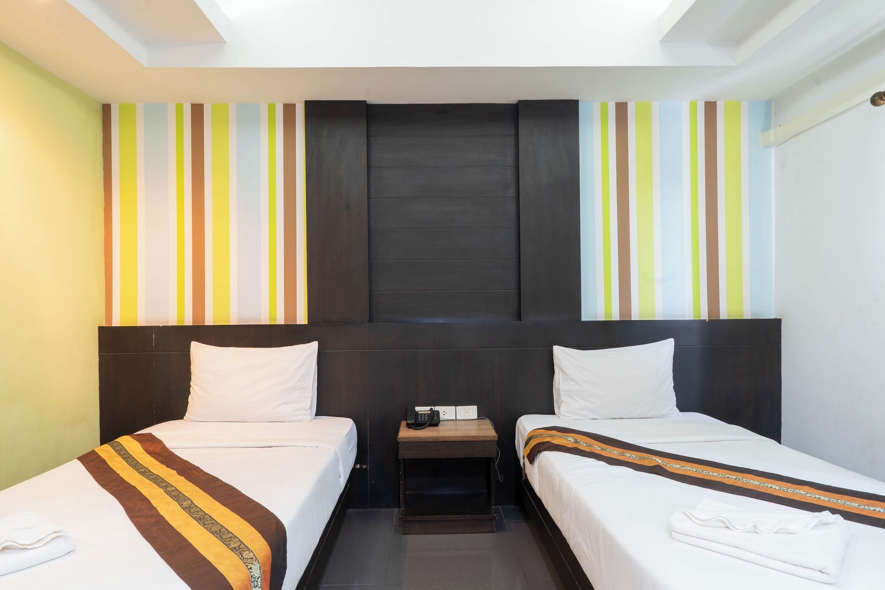 Quarto de hotel com duas camas, uma mesa de cabeceira e uma parede listrada.