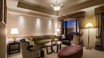 Quarto de hotel com sofá, poltronas, mesa de centro, luminária de chão e vista para o exterior.