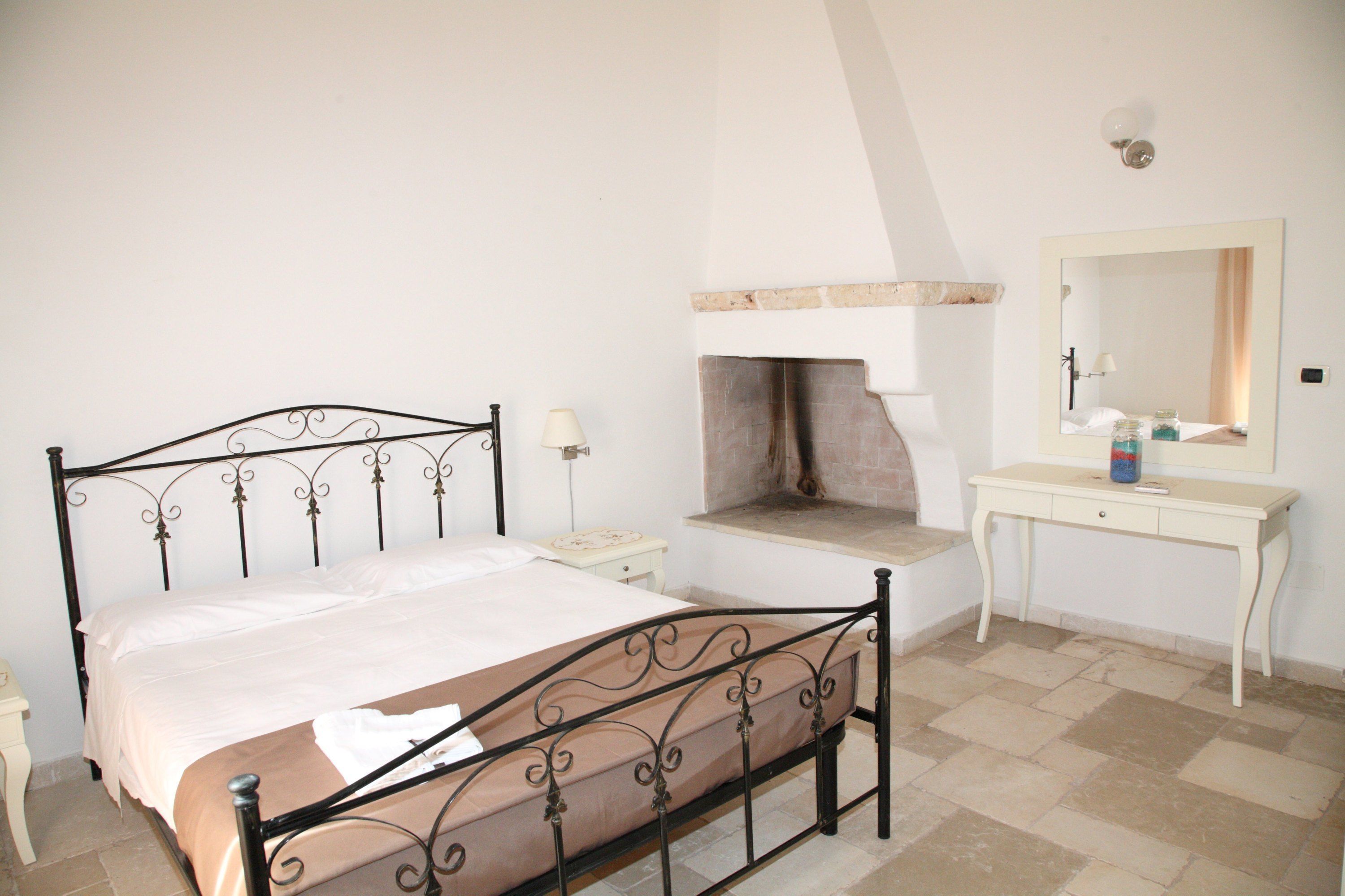 Quarto com cama, mesa de cabeceira, cômoda, espelho e lareira.