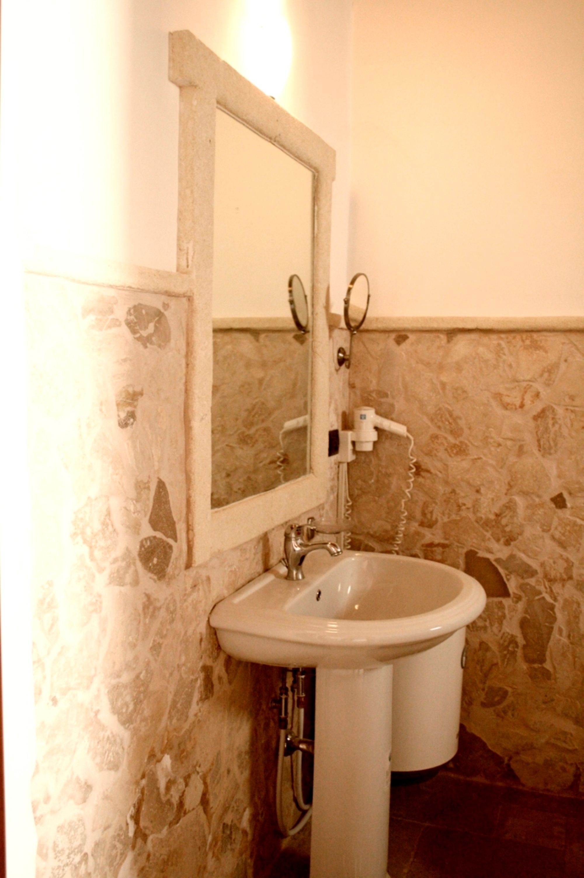 Uma casa de banho com parede de pedra, pia branca e espelho.