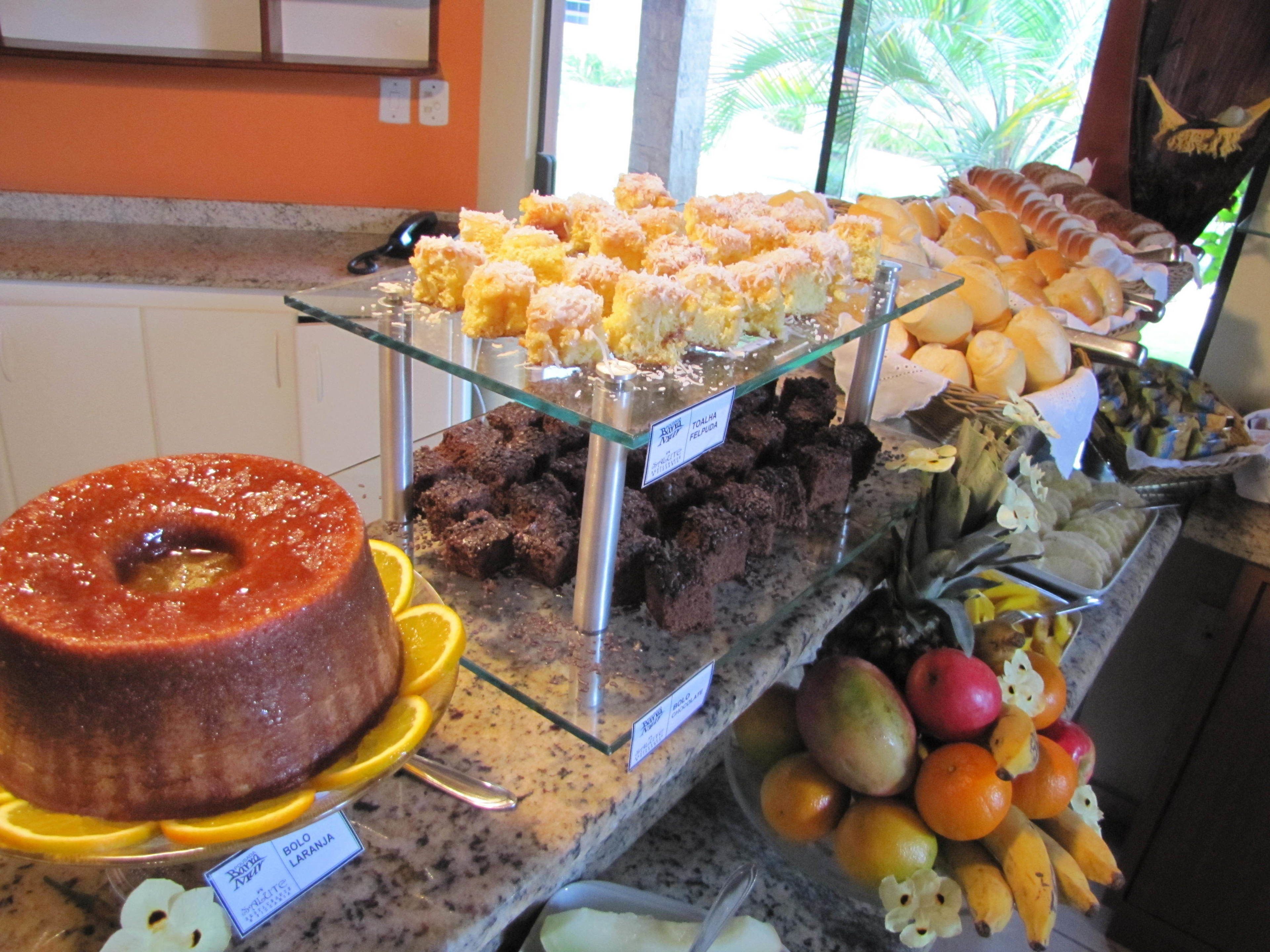 Buffet com diversos alimentos, incluindo bolos, brownies e frutas.