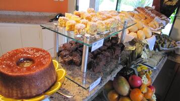Buffet com diversos alimentos, incluindo bolos, brownies e frutas.