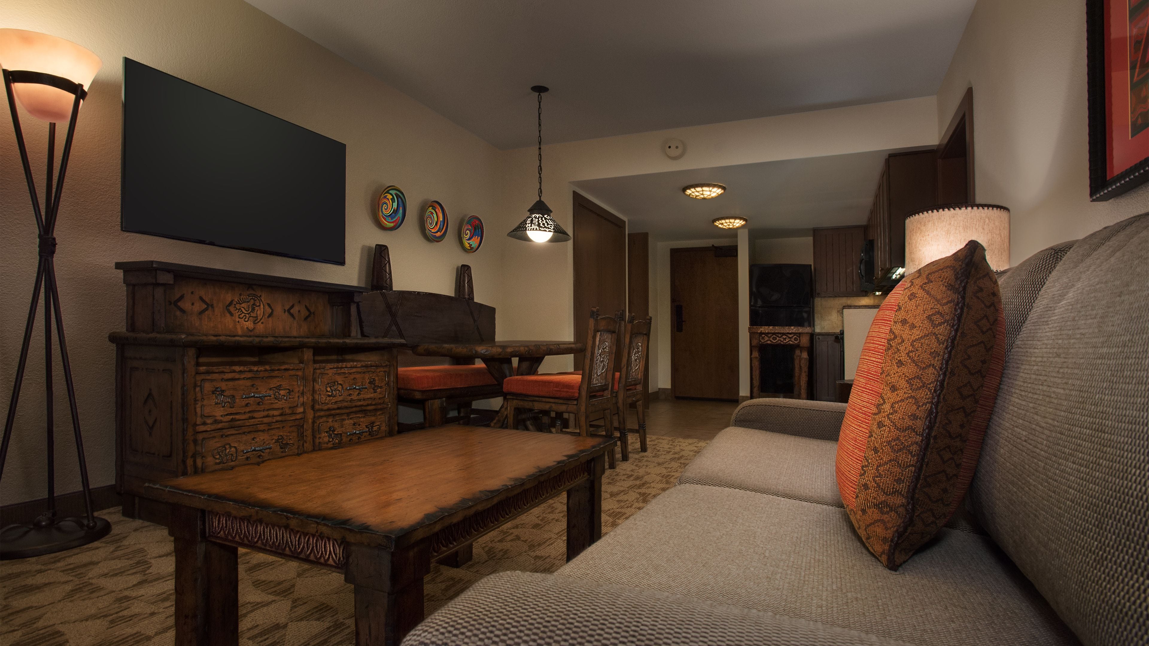 Uma sala de estar aconchegante com uma mesa de centro de madeira, um sofá com almofadas estampadas, uma TV fixada na parede e uma lareira ao fundo.