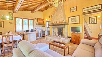 Uma sala de estar acolhedora com lareira, vigas de madeira e uma área de jantar com mesa e cadeiras.