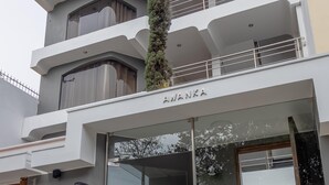 Edifício moderno com entrada de vidro, placa visível e pessoa segurando o puxador da porta.