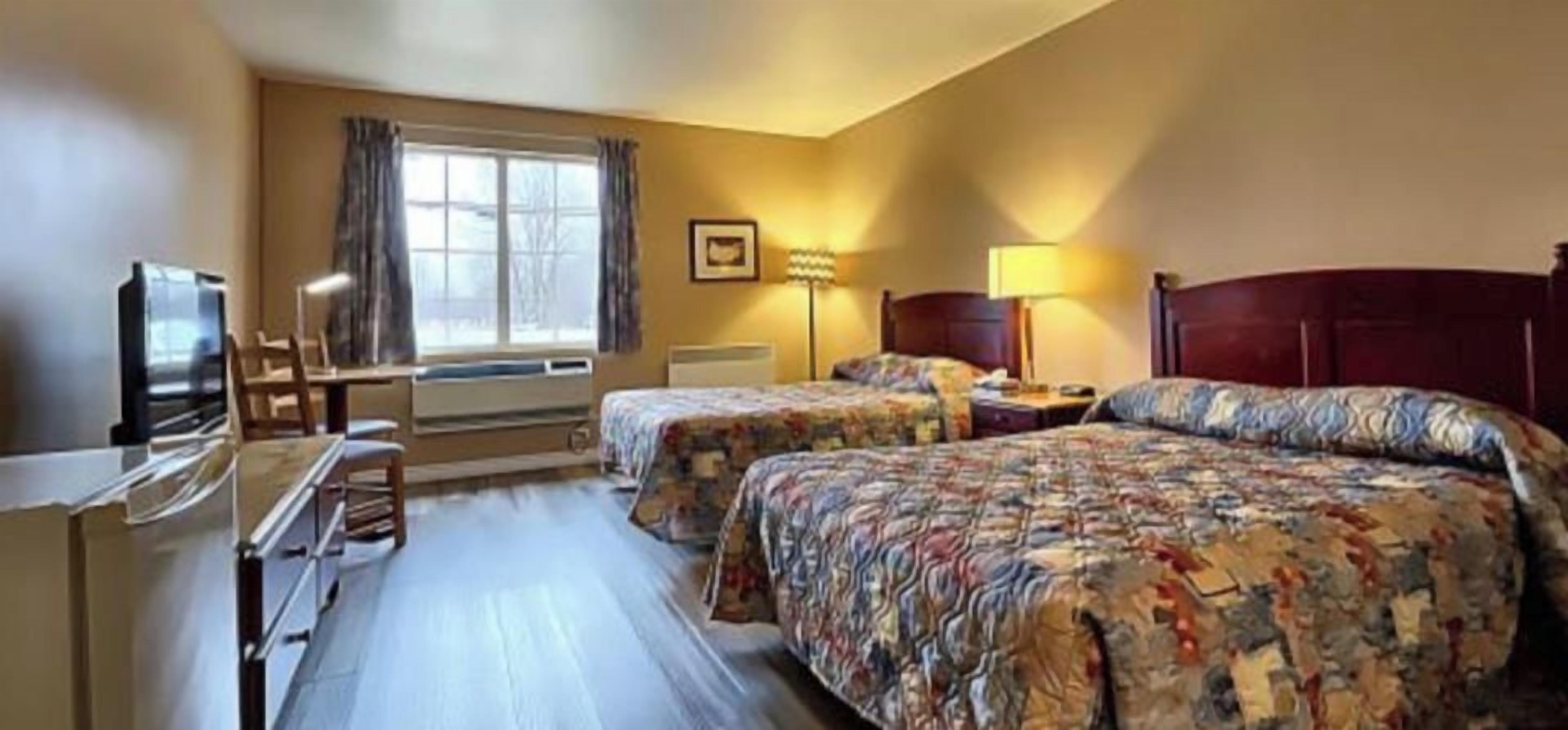 Quarto de hotel com duas camas, uma mesa de trabalho, televisão e janela com cortinas.
