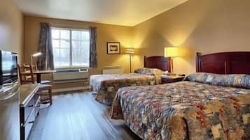 Quarto de hotel com duas camas, uma mesa de trabalho, televisão e janela com cortinas.